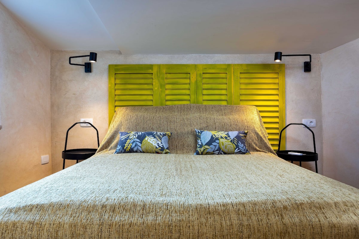 Quarto com cama, duas almofadas, cabeceira e duas luminárias fixadas na parede.