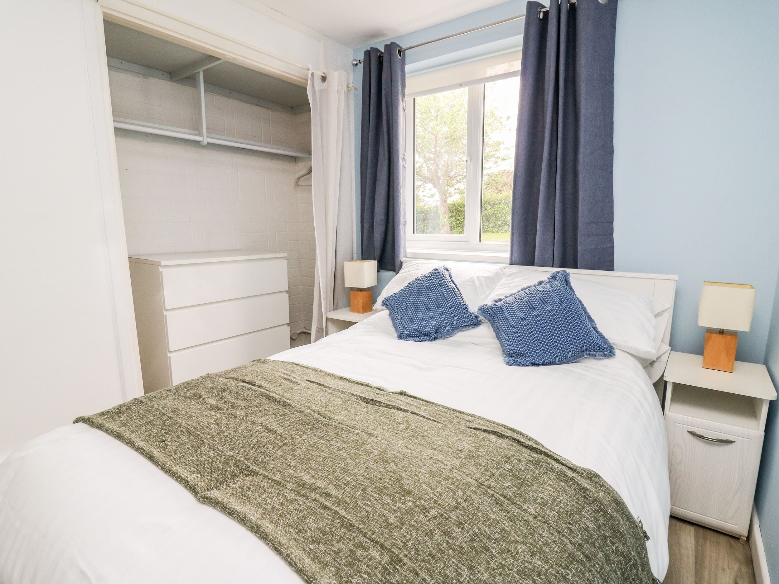 Um quarto com uma cama, duas mesas de cabeceira com abajures, uma janela com cortinas e um guarda-roupa.
