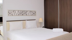 Cama bem arrumada com lençóis brancos, abajur e uma toalha dobrada sobre a cama.