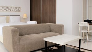 Quarto de hotel moderno com uma cama, um sofá, uma mesa pequena e uma cadeira.