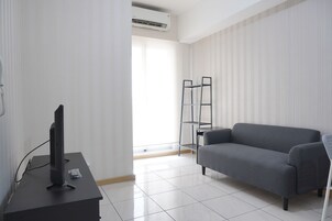 Uma sala de estar moderna com um sofá cinzento, uma TV de tela plana em um suporte preto e um ar condicionado branco na parede.