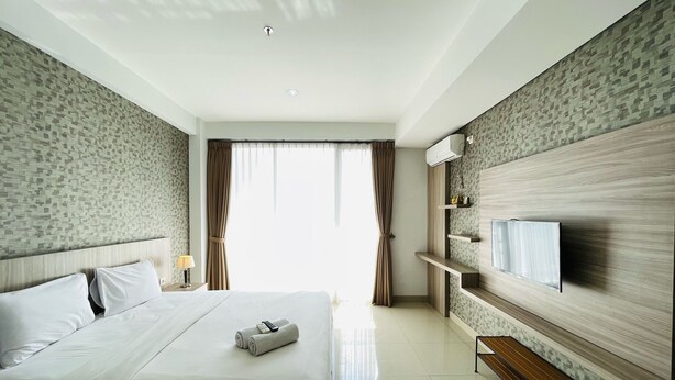 Quarto de hotel moderno com uma cama grande, televisão fixada na parede e janela com cortinas.