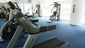 Uma academia com esteiras, aparelhos de musculação e piso revestido de carpete azul.