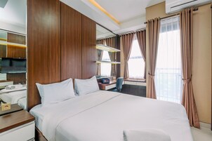 Quarto de hotel com uma cama grande, uma escrivaninha, uma cadeira, uma televisão e uma janela com cortinas.