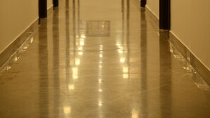 Um corredor com piso lustroso e luminárias na parede.