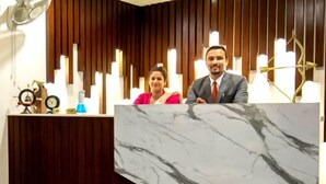 Bancada de recepção com superfície de mármore, painéis de madeira, um ventilador e um vaso de planta.