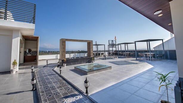 Terraço no telhado com piscina de vidro, áreas de estar e plantas em vasos.