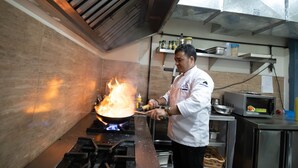 Um cozinheiro preparando comida em um fogão com chamas visíveis.