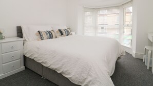 Quarto com cama, mesa de cabeceira, cômoda e janela com persianas.