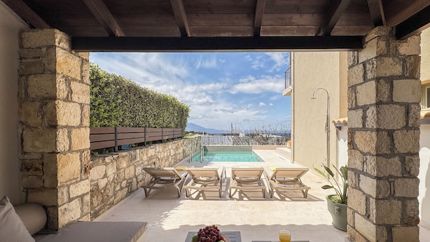 Área da piscina com espreguiçadeiras, uma mesa com frutas e bebidas, e vista para a piscina e montanhas.