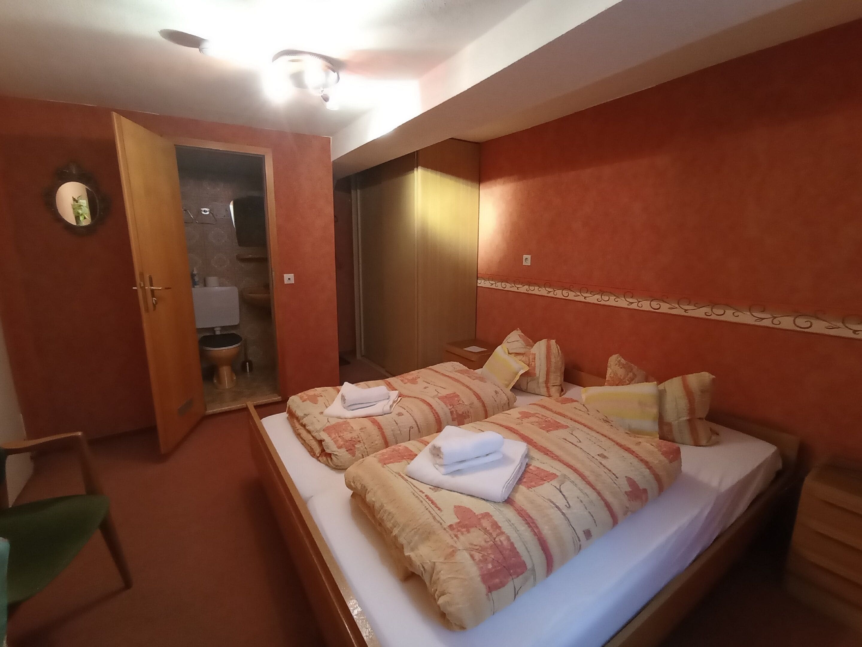 Quarto de hotel com duas camas, um guarda-roupa, uma casa de banho e um espelho.