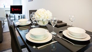 Uma mesa de jantar posta com pratos, tigelas e copos de vinho brancos, e um vaso de flores brancas.