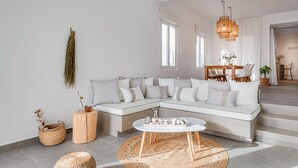 Uma sala de estar moderna com um sofá seccional, uma mesa de centro redonda e um espaço de jantar com mesa e cadeiras de madeira.
