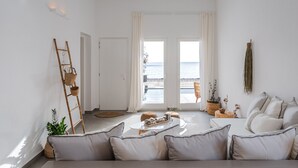 Uma sala de estar ampla com uma grande janela com vista para uma praia, uma escada de madeira e um espaço de estar acolhedor.