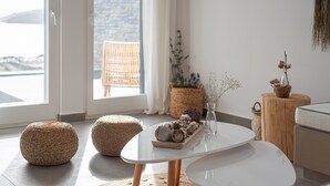 Uma sala de estar moderna com uma mesa branca, pufes de vime, um cesto de vime e vista para o exterior através de uma grande janela.