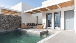 Uma área de piscina moderna ao ar livre, com paredes de pedra, cadeiras de vime e um espaço de estar com almofadas.