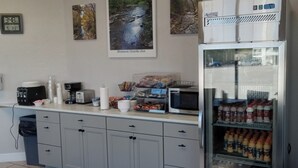 Uma cozinha compacta com cafeteira, torradeira, micro-ondas e geladeira repleta de bebidas.
