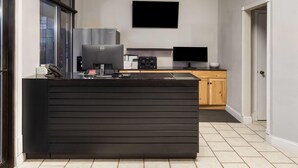 Cozinha moderna com bancada preta, TV de tela plana na parede e máquina de café.