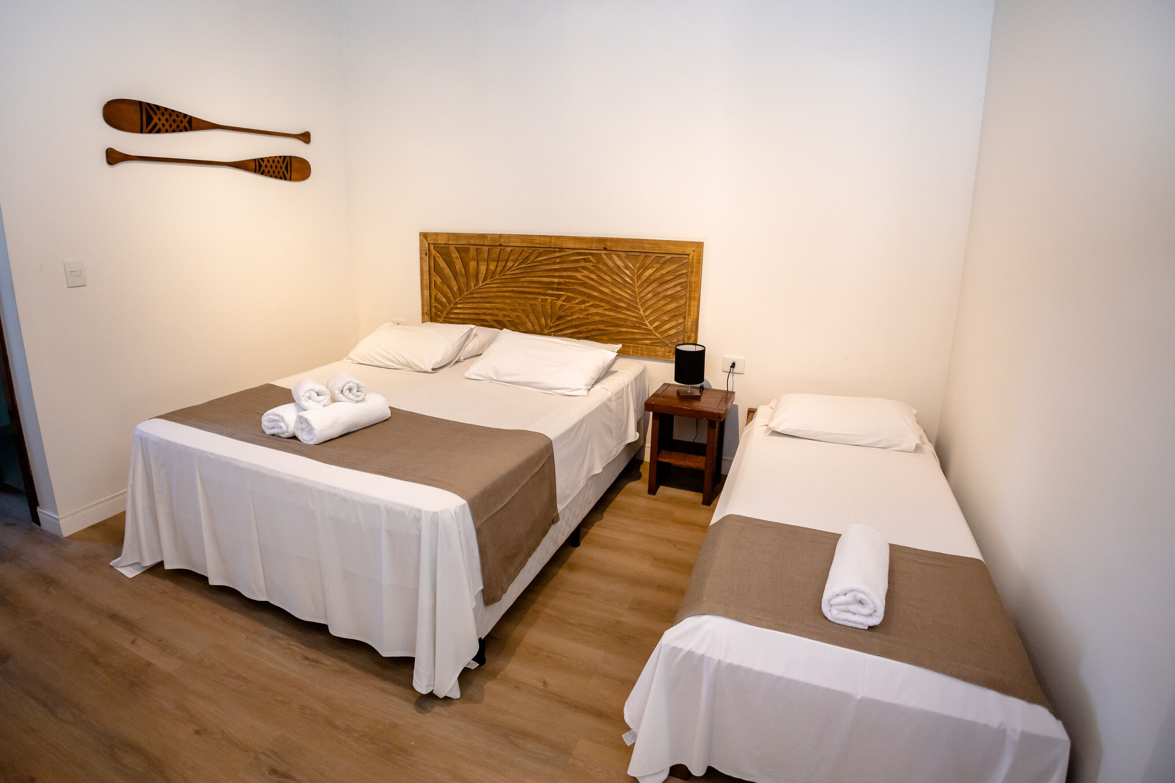 Quarto de hotel com duas camas, uma cabeceira de madeira e dois painéis de madeira na parede.