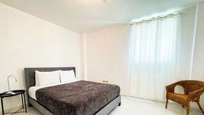 Quarto com cama, mesa de cabeceira, cadeira e janela com cortinas.