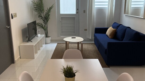 Uma sala de estar moderna com uma mesa de jantar branca, um sofá azul e um ventilador de teto.