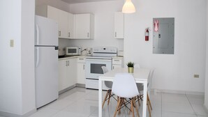 Uma cozinha moderna com armários brancos, geladeira, micro-ondas, forno e uma mesa de jantar com cadeiras.