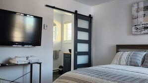 Quarto com cama, televisão presa à parede, porta deslizante e pintura na parede.