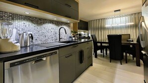 Uma cozinha moderna equipada com lava-louças, chaleira e máquina de café. Há uma área de refeições com mesa e cadeiras.