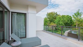 Uma varanda com móveis de vime, guarda-corpo de vidro e vista para o verde.