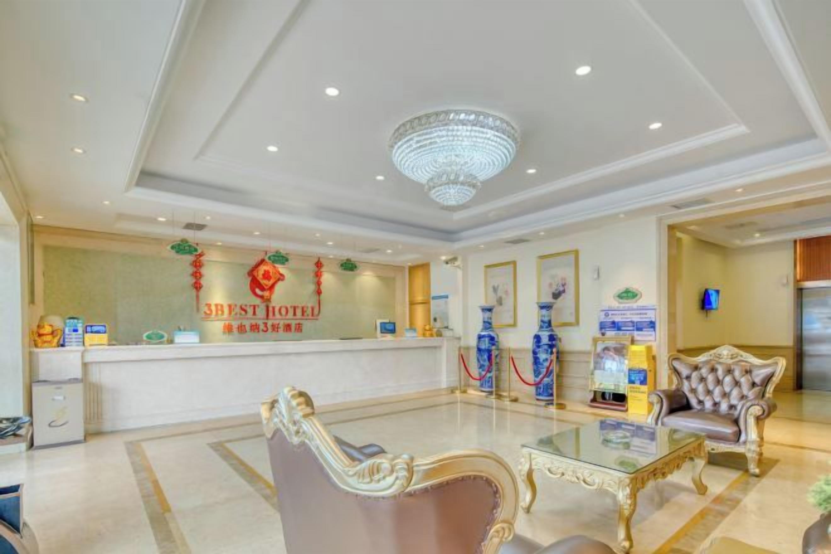 Um saguão de hotel com balcão de recepção, um candelabro, uma poltrona confortável e uma mesa de centro.