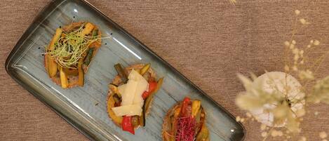 Prato retangular com três tipos diferentes de comida, um garfo e um vaso com flores secas sobre uma superfície texturizada.