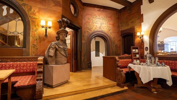 Interior de restaurante com painéis de madeira, decorações elaboradas nas paredes e uma estátua como peça central.