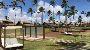 Resort com áreas de estar ao ar livre, palmeiras e céu claro.