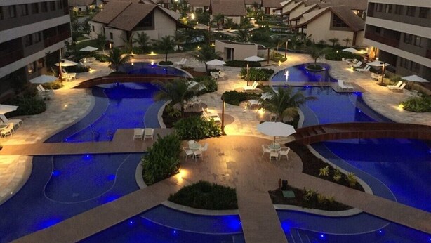 Resort com várias piscinas, palmeiras e vista para a praia.