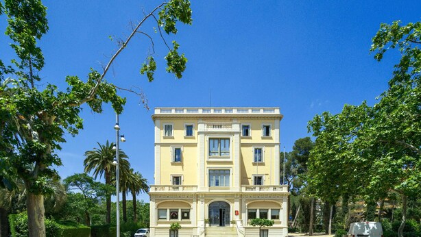 Um edifício de vários andares com fachada simétrica, grandes janelas e entrada central com degraus.