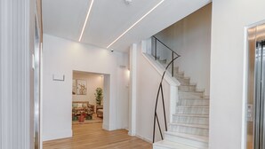 Um interior moderno com piso de madeira, escada com corrimão de vidro e área de estar com sofá e mesa de centro.