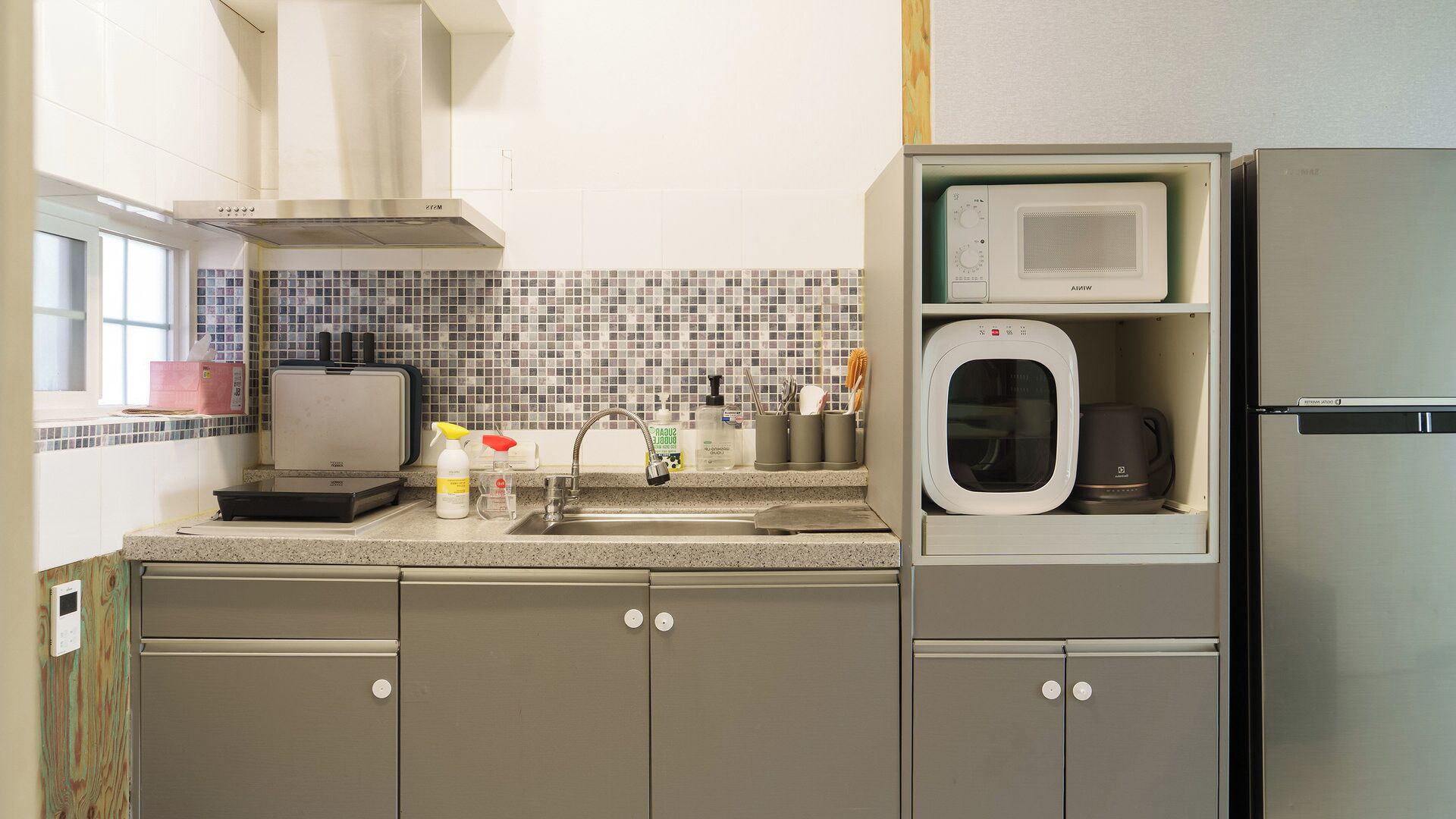 Uma cozinha compacta com micro-ondas, pia e geladeira de aço inoxidável.