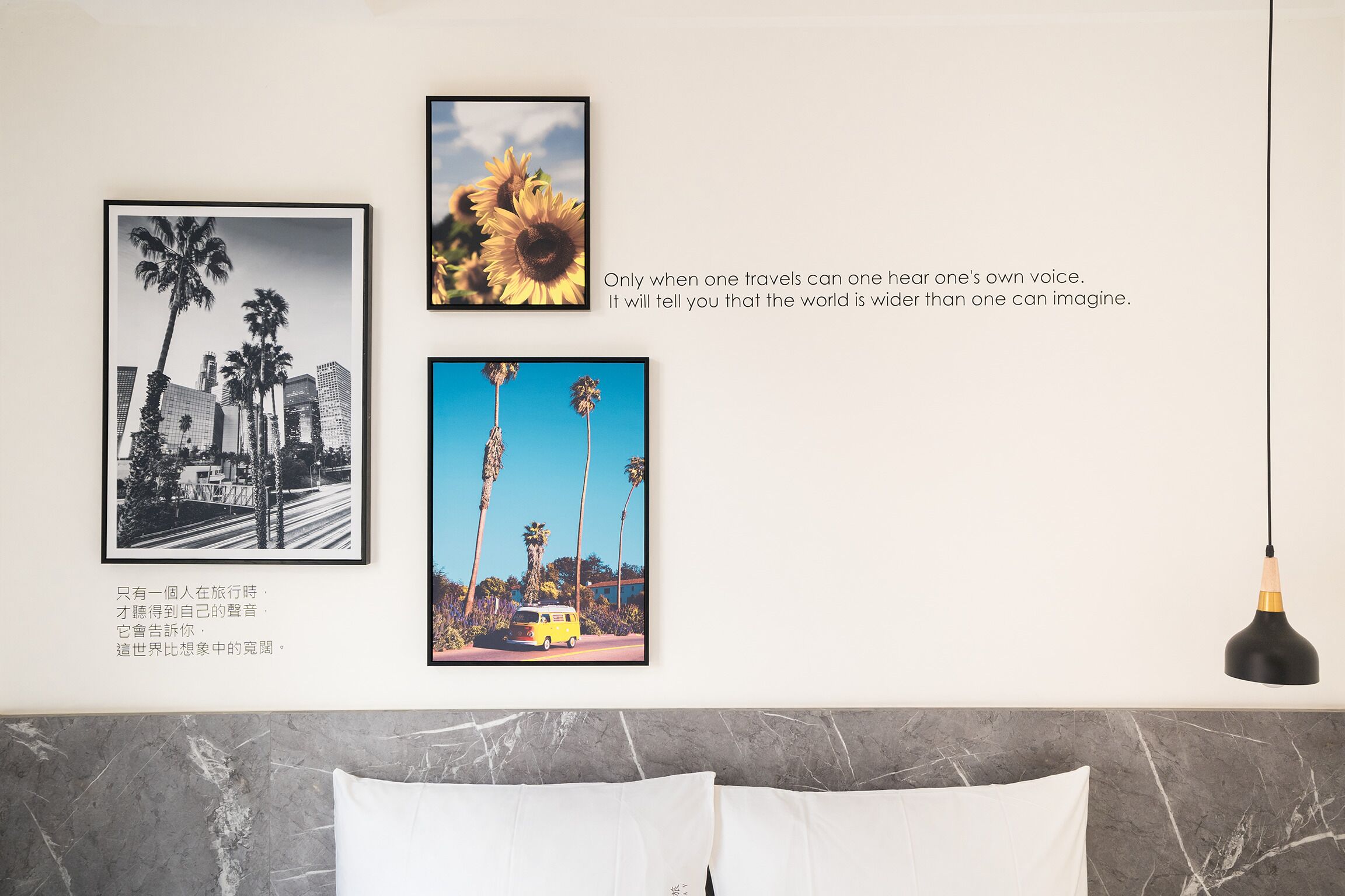 Quarto de hotel com cama, cabeceira de mármore e três quadros na parede.