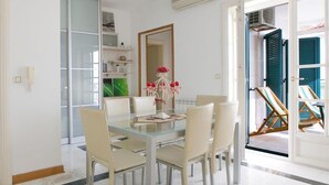 Uma sala de jantar com mesa e cadeiras de vidro, um arranjo decorativo e vista para uma varanda com cadeiras.