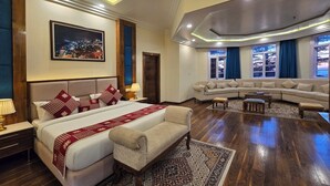 Quarto de hotel espaçoso com uma cama grande, um sofá e vista para a cidade à noite.