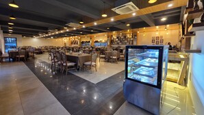 Um restaurante amplo com pé-direito alto, iluminação pendente e um balcão central de exposição.