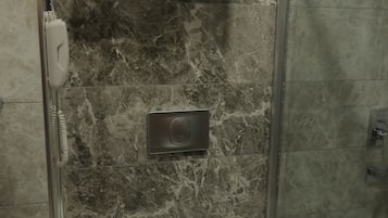 Um banheiro com box de vidro, paredes de mármore, vaso sanitário com tampa branca e porta-toalhas com duas toalhas.