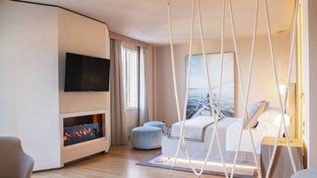 Quarto de hotel moderno com TV de tela plana, lareira, cama com vista para o mar e luminária pendente em corda.
