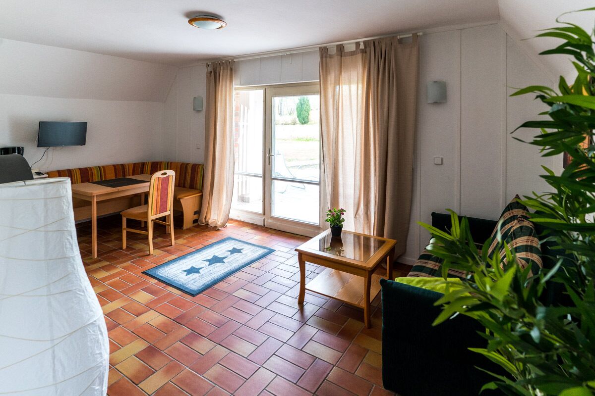 Quarto com cama, escrivaninha, poltrona, sofá, televisão e janela com cortinas.