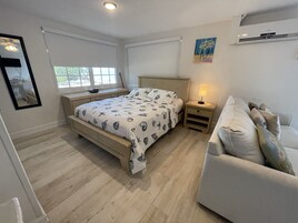 Quarto com cama, mesa de cabeceira, luminária e sofá.