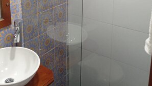 Casa de banho com chuveiro em cabine de vidro, lavatório branco e azulejos padronados em azul e amarelo.