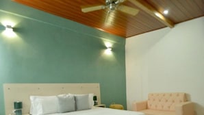 Quarto com cama, um banquinho, mesa de cabeceira, abajur e ventilador de teto.