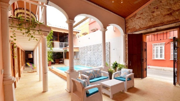 Área externa coberta com móveis de vime branco, piscina e uma parede de pedra.