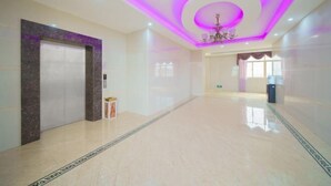 Um corredor amplo com piso de mármore, um lustre central e uma porta com moldura de mármore.