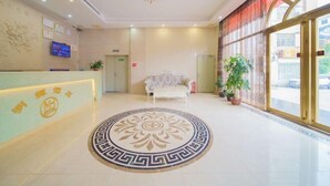 Um hall de hotel com balcão de recepção, piso estampado, sofá e uma janela grande.